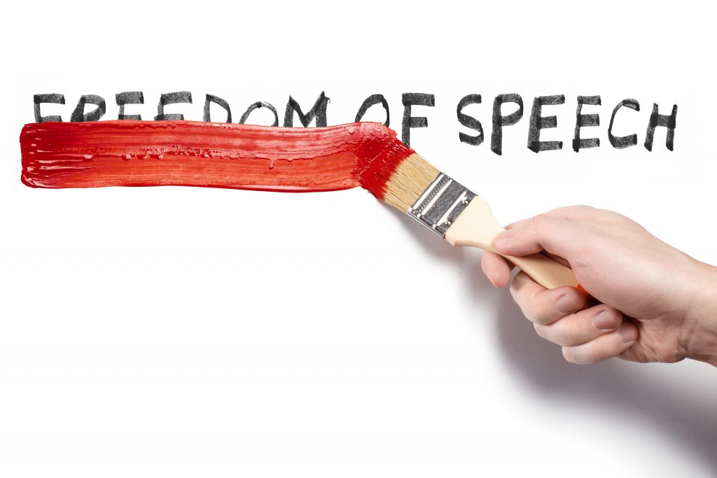 Hand painting over the words "Freedom of speech" using a red brush ...